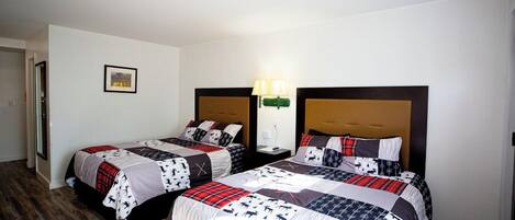 Quarto de hotel com duas camas, cada uma com cabeceira, mesa de cabeceira e luminária.