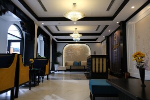 Um hall com sofá, cadeiras, mesa de centro, balcão de recepção e lustre.