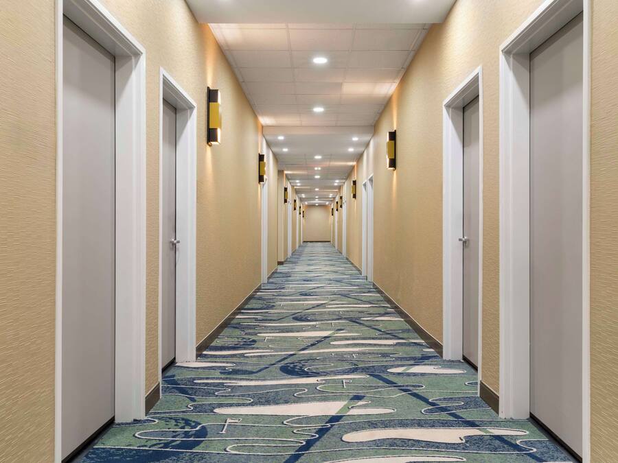 Um corredor de hotel com carpete estampado, portas brancas e iluminação embutida.
