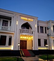 Uma imponente entrada de hotel com uma grande porta em arco, um tapete vermelho que conduz aos degraus, e uma placa com a inscrição "HOTEL DALLI SAMARKAND".