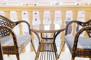 Cadeiras de vime e uma mesa numa varanda com vista para edifícios.