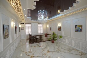 Um hall amplo com piso de mármore, um lustre imponente e uma escadaria com guarda-corpo de madeira.
