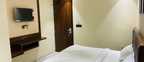 Quarto de hotel com cama, ventoinha no teto, televisão fixada na parede e guarda-roupa de madeira.