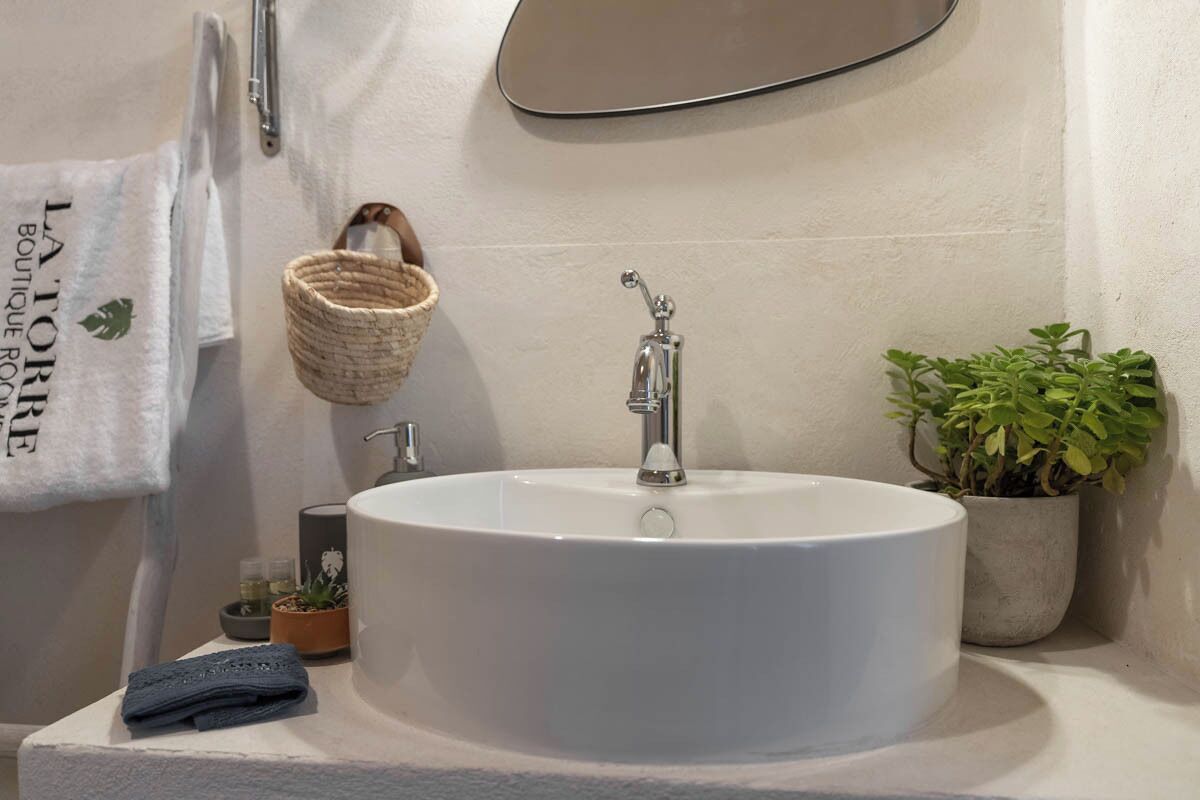 Casa de banho com lavatório branco, cesto suspenso, planta em vaso e um porta-toalhas com toalha.