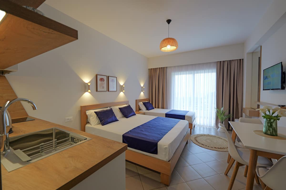 Quarto de hotel com duas camas, área de cozinha com pia, mesa de jantar e televisão.