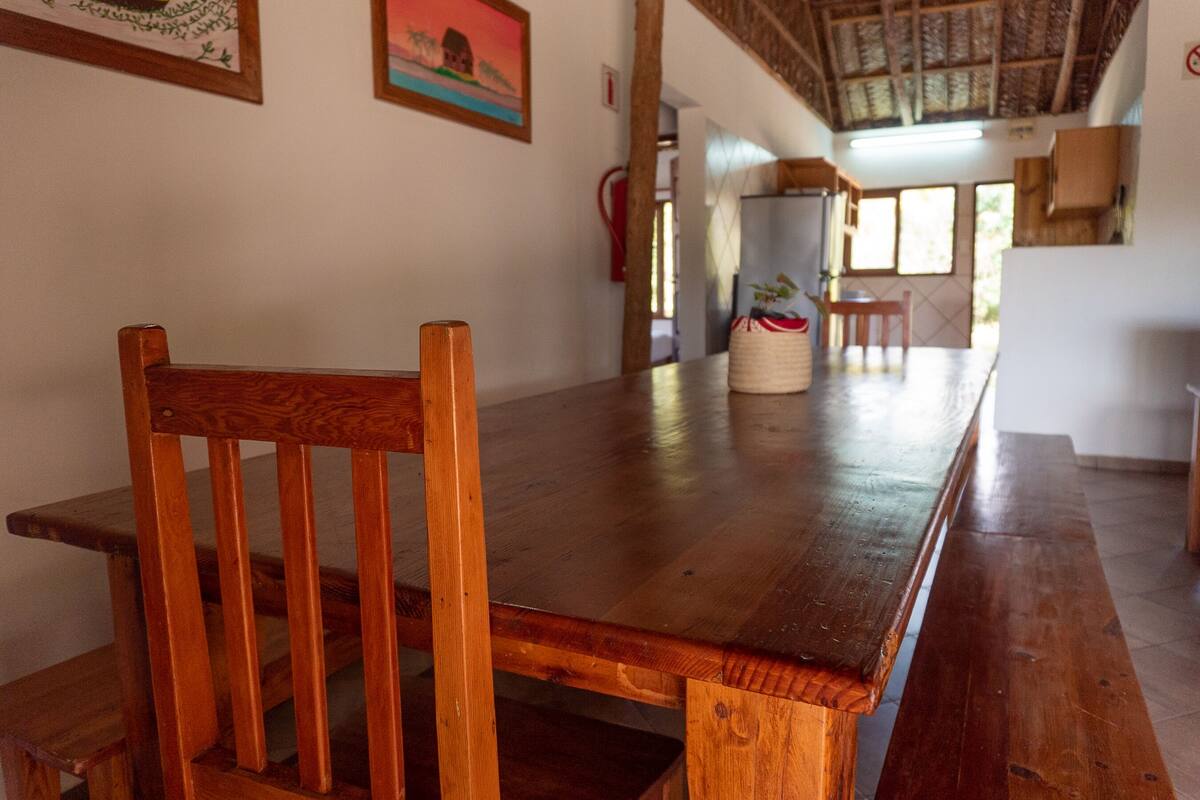 Uma mesa de jantar de madeira com cadeiras em um quarto com paredes brancas e um telhado de palha.