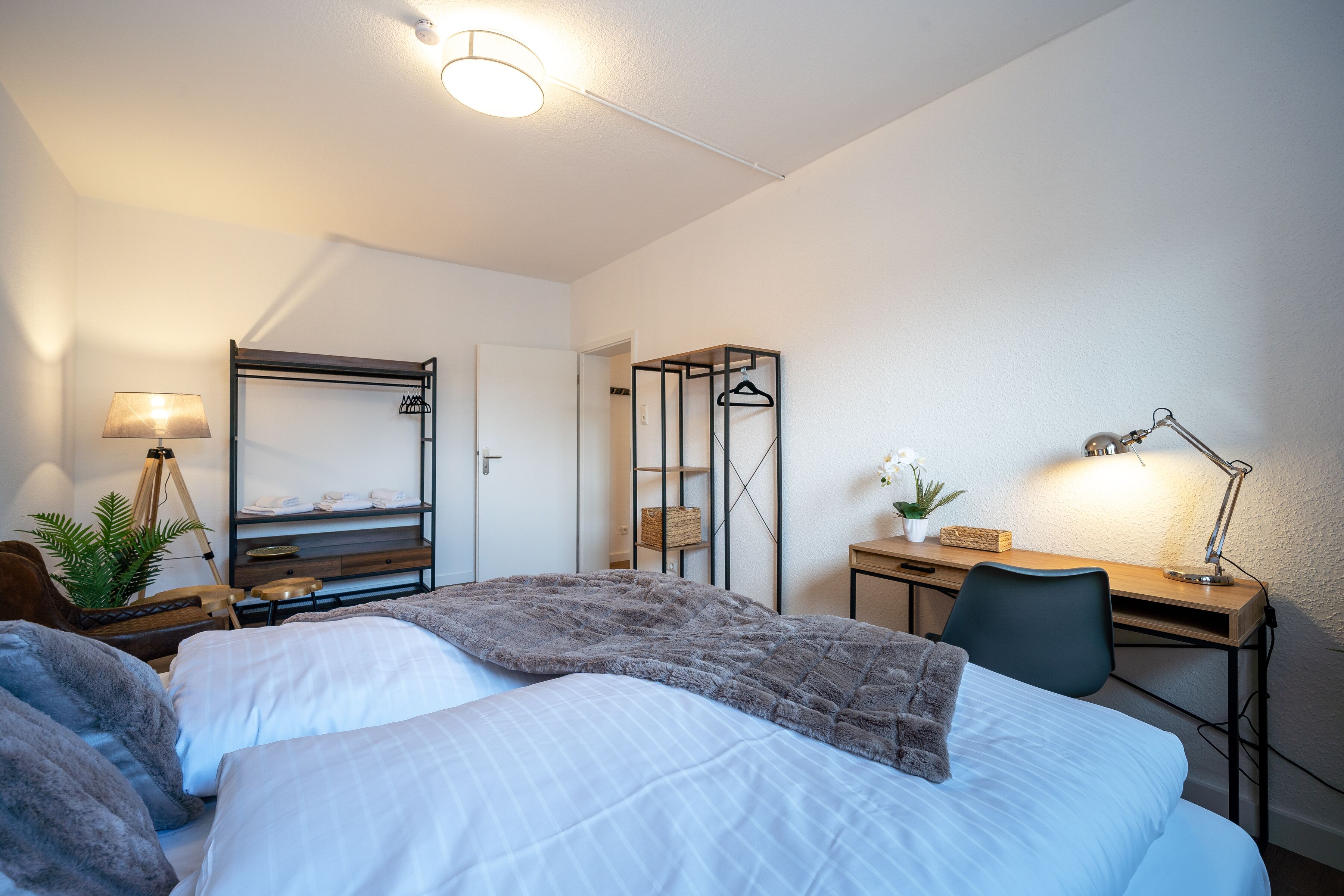 Quarto com cama, escrivaninha, cadeira, abajur e guarda-roupa.