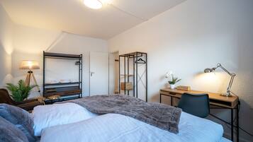 Quarto com cama, escrivaninha, cadeira, abajur e guarda-roupa.