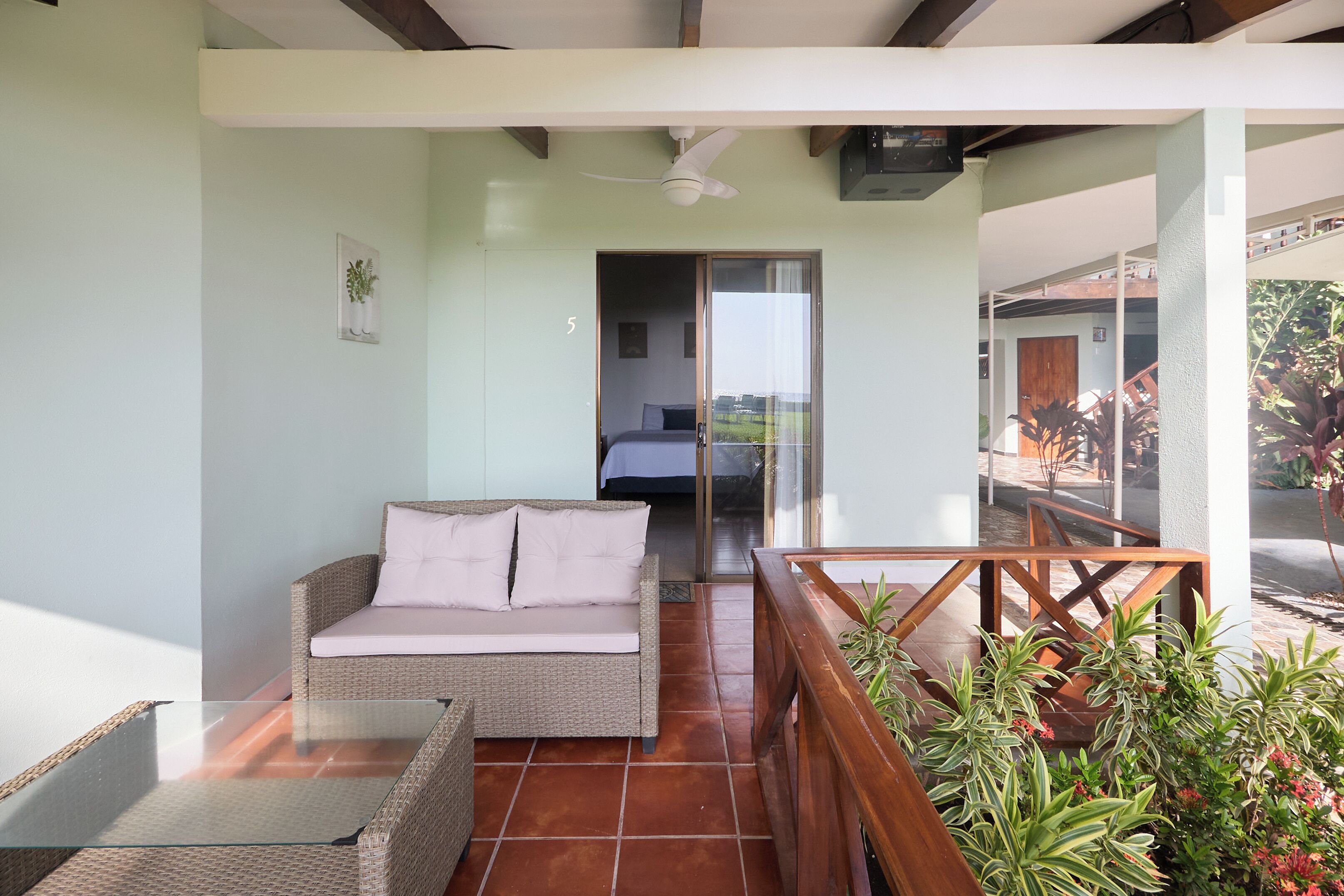 Uma varanda com móveis de vime, um ventilador de teto e vista para o jardim.