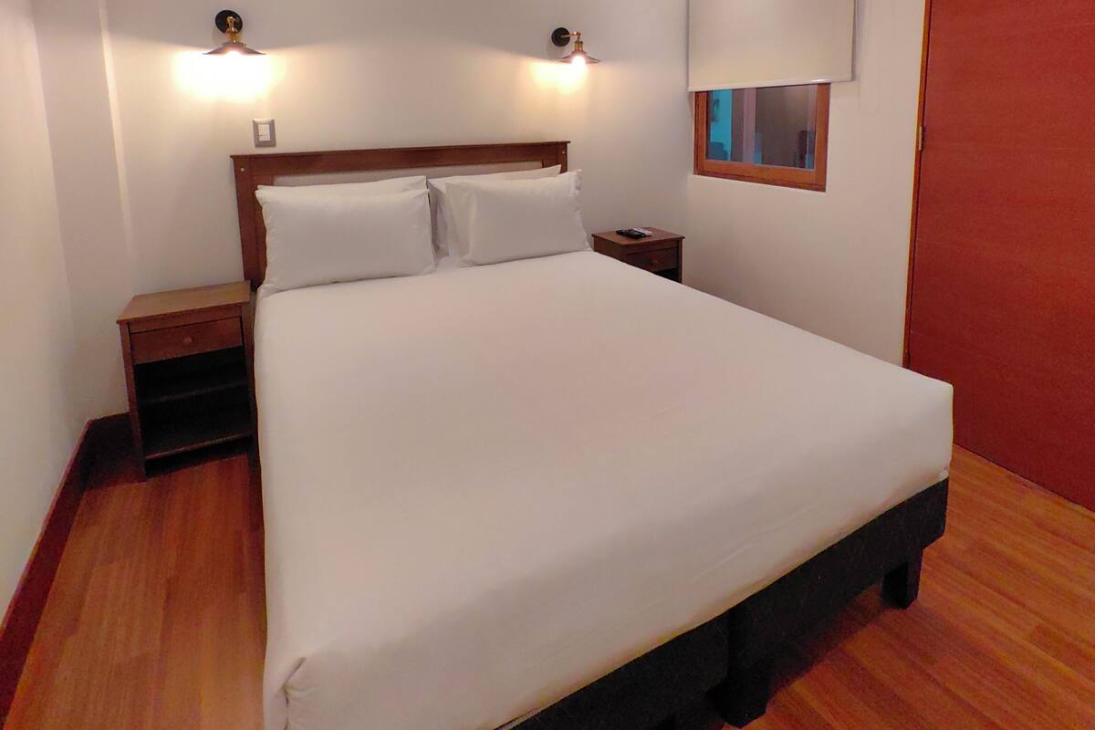 Quarto de hotel bem arrumado com uma cama grande, mesas de cabeceira e iluminação fixada na parede.