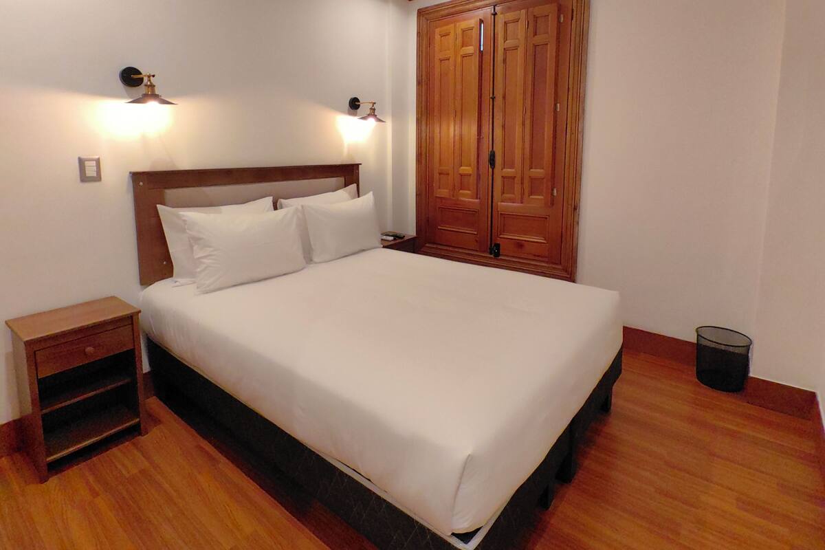 Quarto com uma cama grande, guarda-roupa de madeira, abajures e uma pequena mesa de cabeceira.