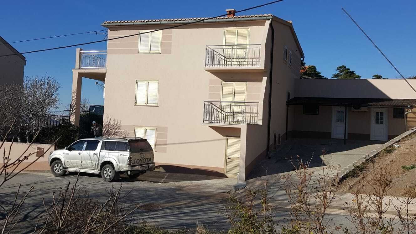 Um edifício com várias andares e varandas, um SUV branco estacionado e céu claro.