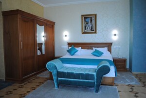 Quarto com uma cama grande, guarda-roupa de madeira, um banco e um quadro na parede.