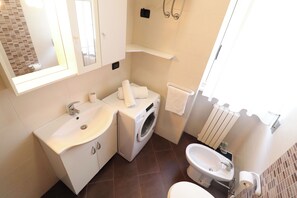 Casa de banho compacta com lavatório, sanita e máquina de lavar roupa.