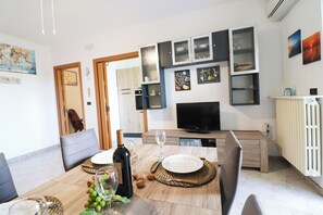 Uma sala de jantar com uma mesa de madeira posta para dois, uma televisão e armários fixados na parede.