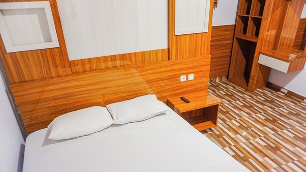 Quarto de hotel com cabeceira de madeira, cama com roupa de cama branca, mesa de cabeceira e controle remoto, e piso estampado.