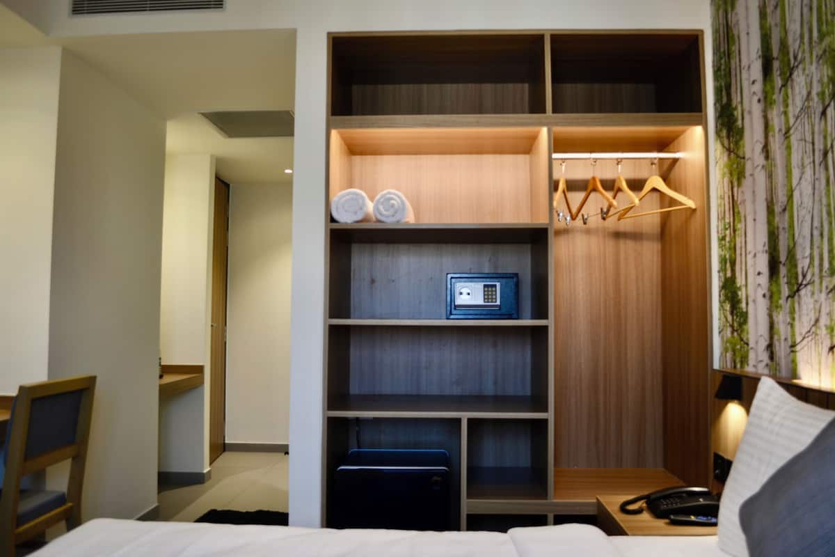 Quarto de hotel com guarda-roupa de madeira, uma cama, uma escrivaninha e uma luminária na parede.