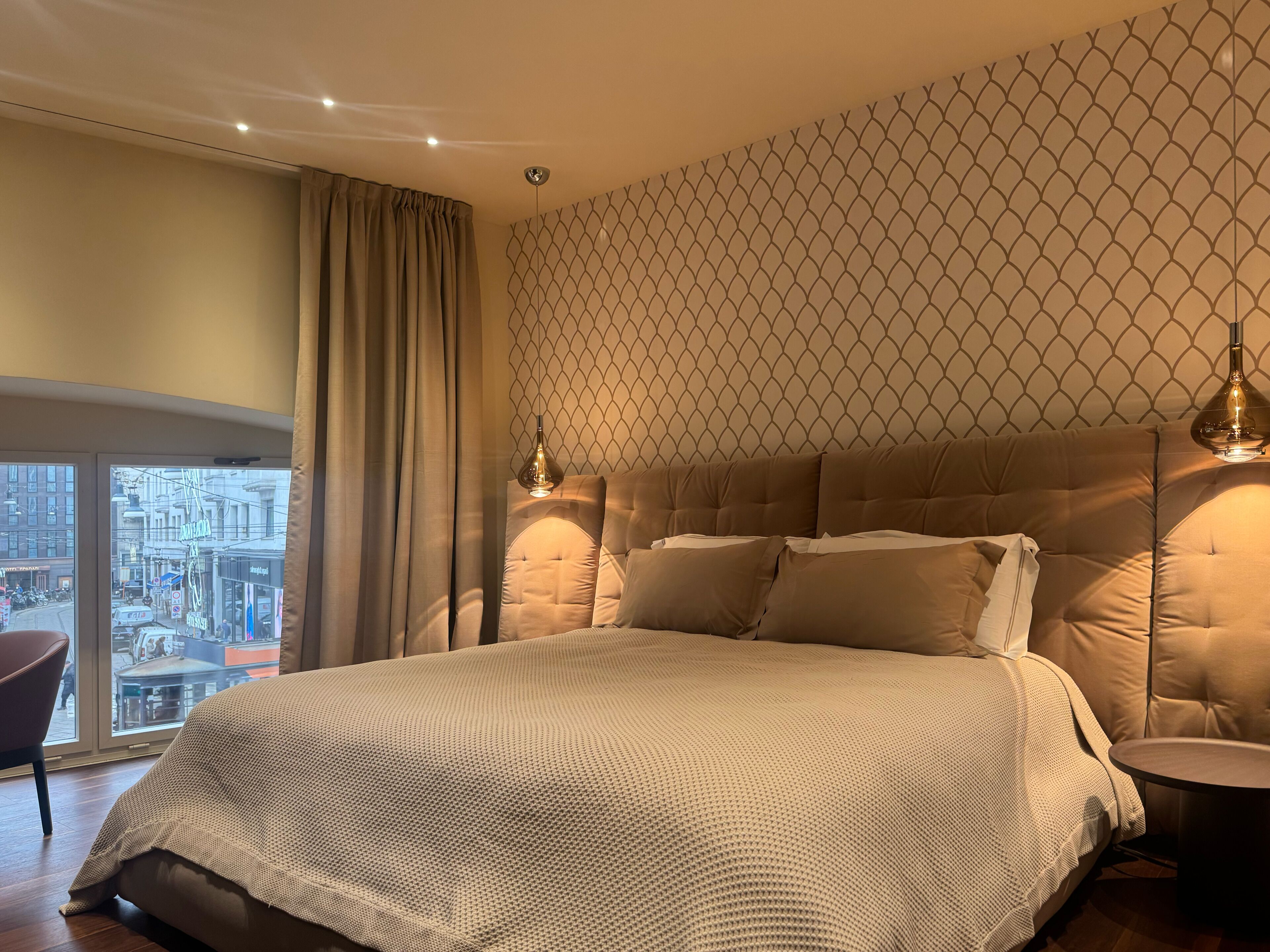 Quarto com cama grande, vista da cidade pela janela e parede com padrão.