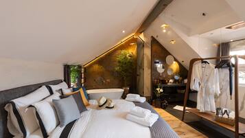 Quarto de hotel moderno com uma cama grande, teto de madeira e banheiro visível ao fundo.