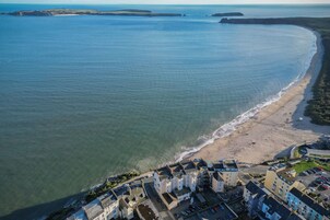 Vista aérea de uma cidade costeira com uma praia de areia, mar azul límpido e edifícios ao longo da costa.