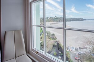 Quarto com uma janela ampla de frente para a praia, uma cadeira e móveis de exterior.