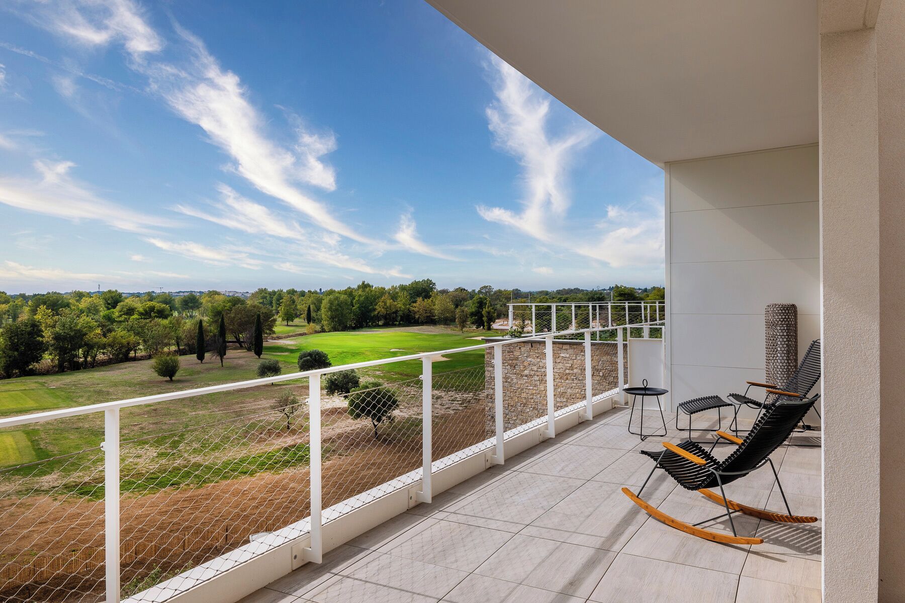 Varanda com vista para um campo de golfe, corrimão branco e duas cadeiras de balanço.