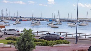 Uma marina com barcos atracados, uma rua com carros estacionados e um céu claro.