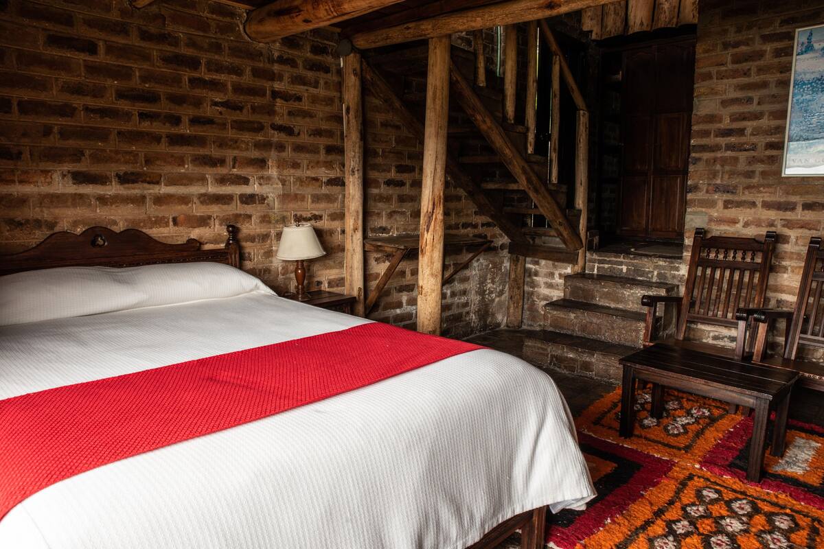 Quarto com cama grande, escada de madeira e paredes de tijolos rústicos.