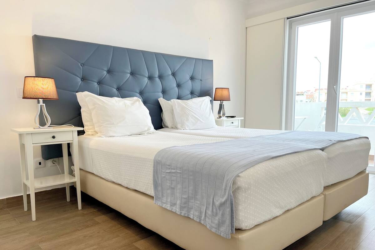 Quarto com uma cama grande, duas mesinhas de cabeceira e uma janela com vista.