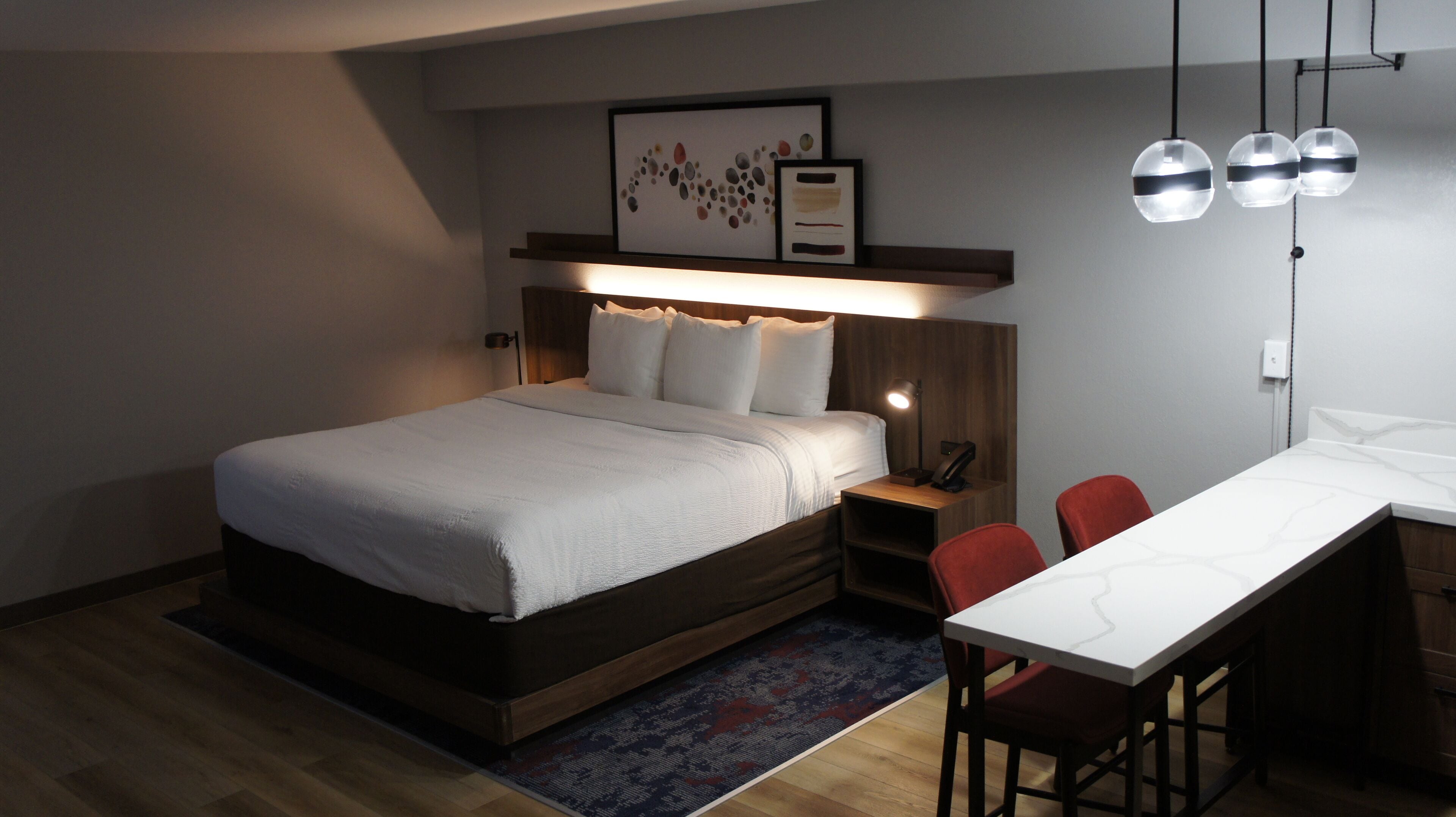 Quarto de hotel moderno com uma cama grande, uma escrivaninha com cadeira e uma mesa pequena.