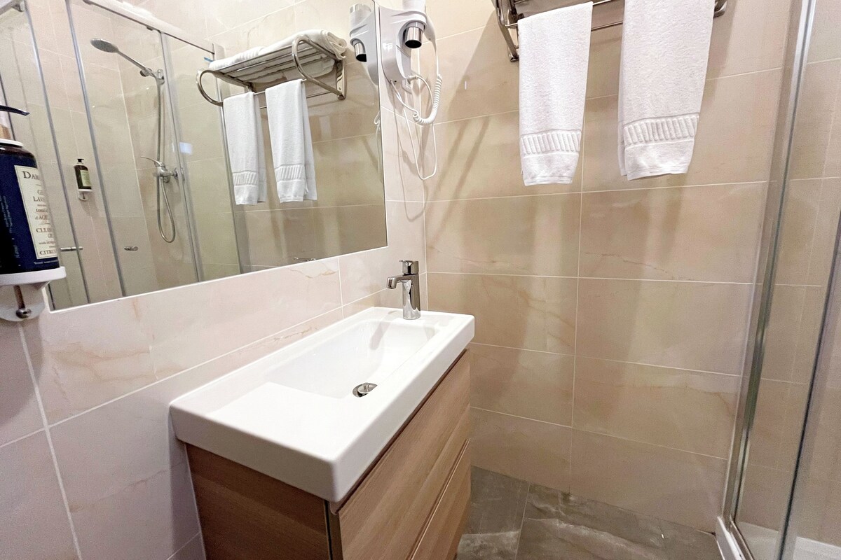 Casa de banho moderna com um espelho grande, lavatório, cabine de duche em vidro e duas toalhas penduradas numa barra.
