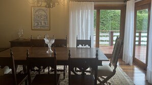 Uma sala de jantar com um candelabro, uma obra de arte emoldurada e vista para um deck de madeira através de uma porta de vidro.