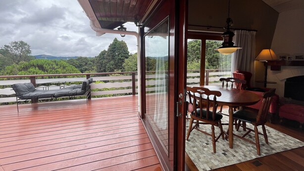 Um deck de madeira com vista para um lago e árvores, uma área de refeições com mesa e cadeiras, e um sofá.