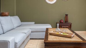 Uma sala de estar com um sofá cinza claro, uma mesa de centro de madeira com um jogo americano trançado e três pratos decorativos fixados na parede.