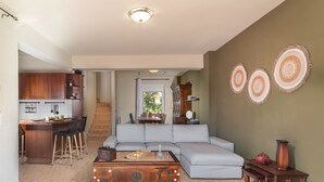 Uma sala de estar com sofá, mesa de centro de madeira e área de cozinha com armários de madeira e balcão.