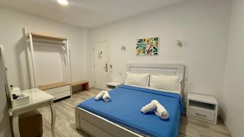 Quarto de hotel moderno com uma cama, uma escrivaninha, um guarda-roupa e uma pequena mesa de cabeceira.