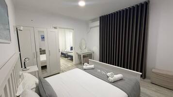 Quarto de hotel moderno com uma cama grande, mesa de cabeceira, espelho e vista para o banheiro.