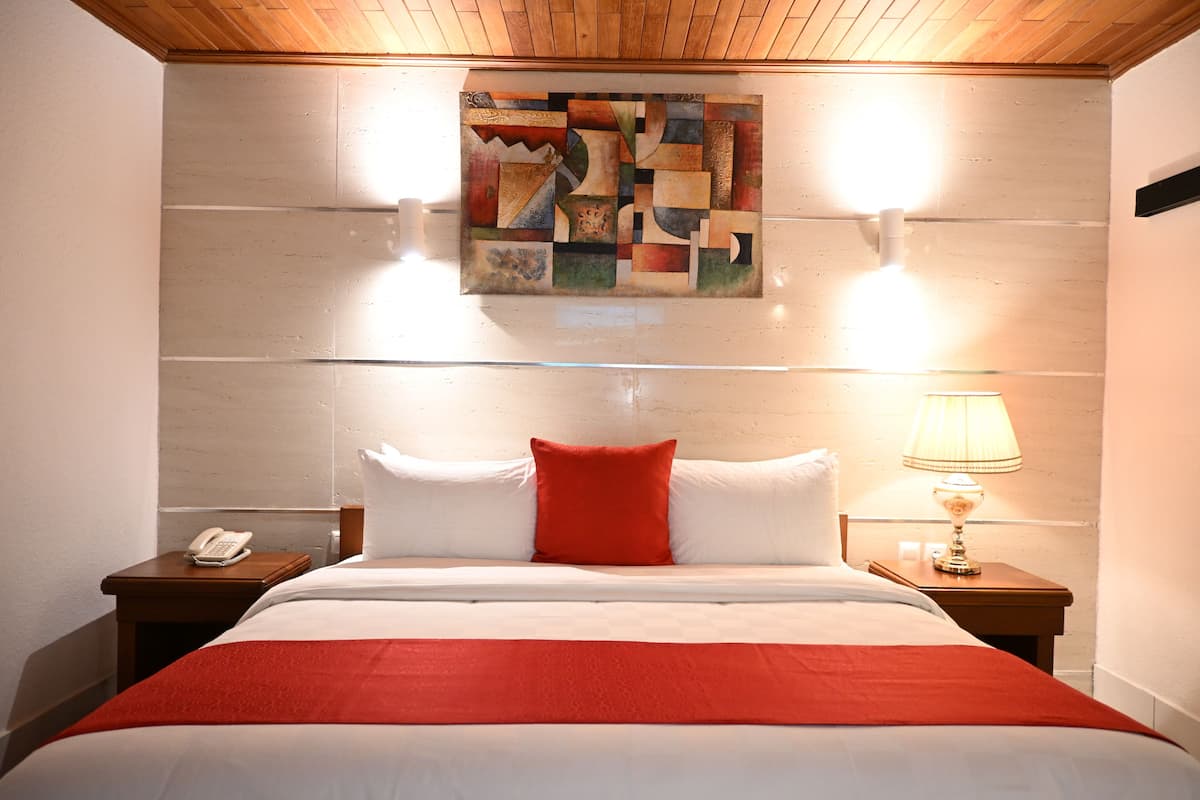 Quarto de hotel com cama, telefone, abajur e uma obra de arte na parede.