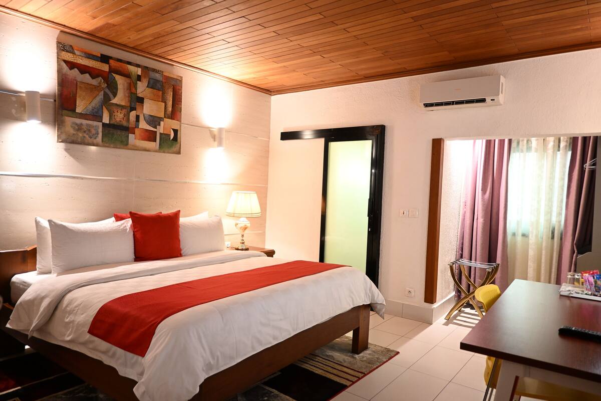 Quarto de hotel com cama, mesa, luminária e aparelho de ar condicionado.