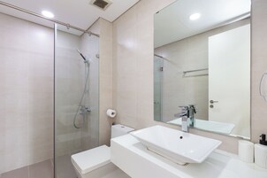 Uma casa de banho moderna com chuveiro envidraçado, lavatório branco e espelho grande.