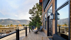 Um deck de madeira com lareira, área de estar ao ar livre e grandes janelas com vista para as montanhas.