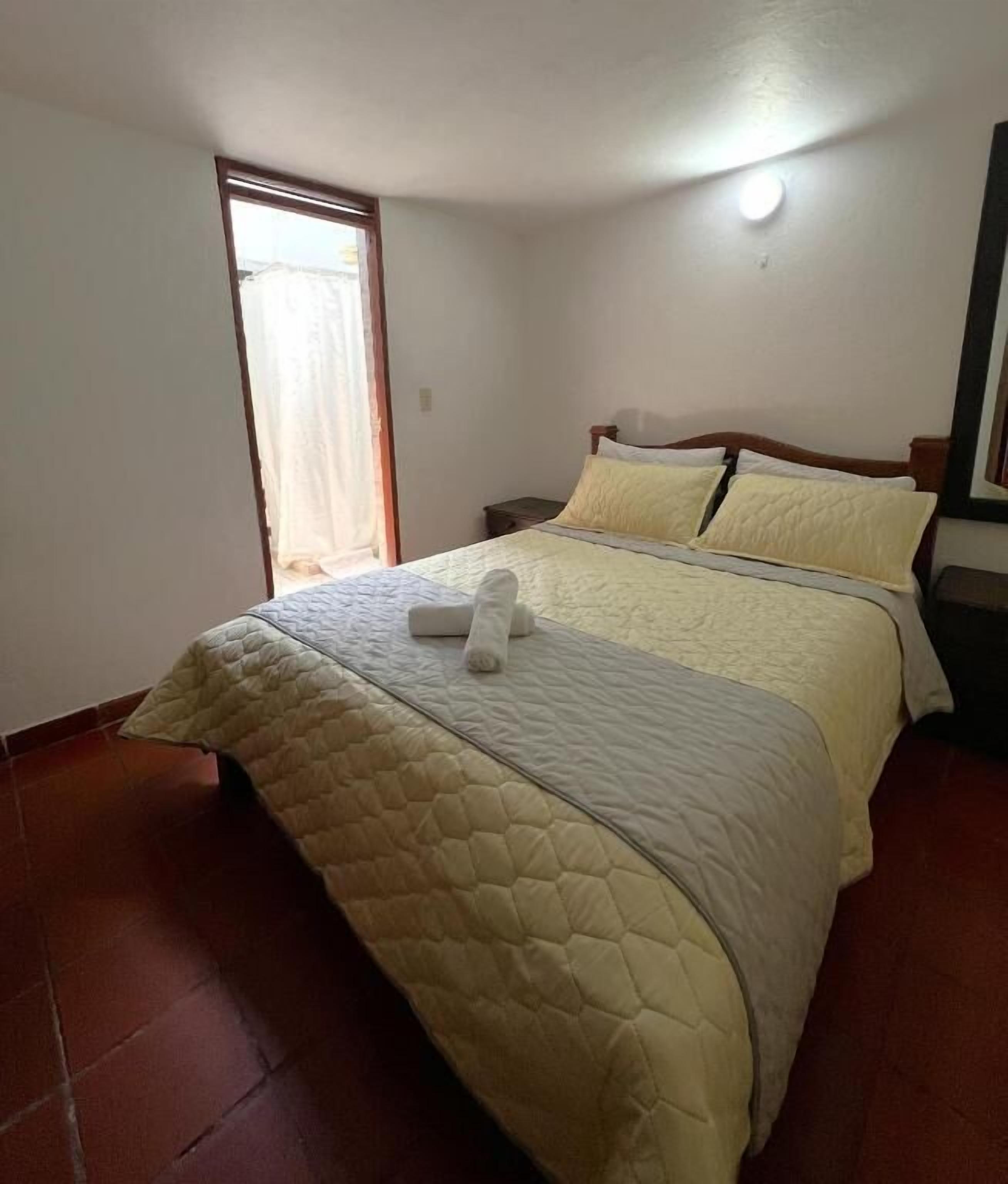 Quarto com cama, mesa de cabeceira e janela com cortinas.
