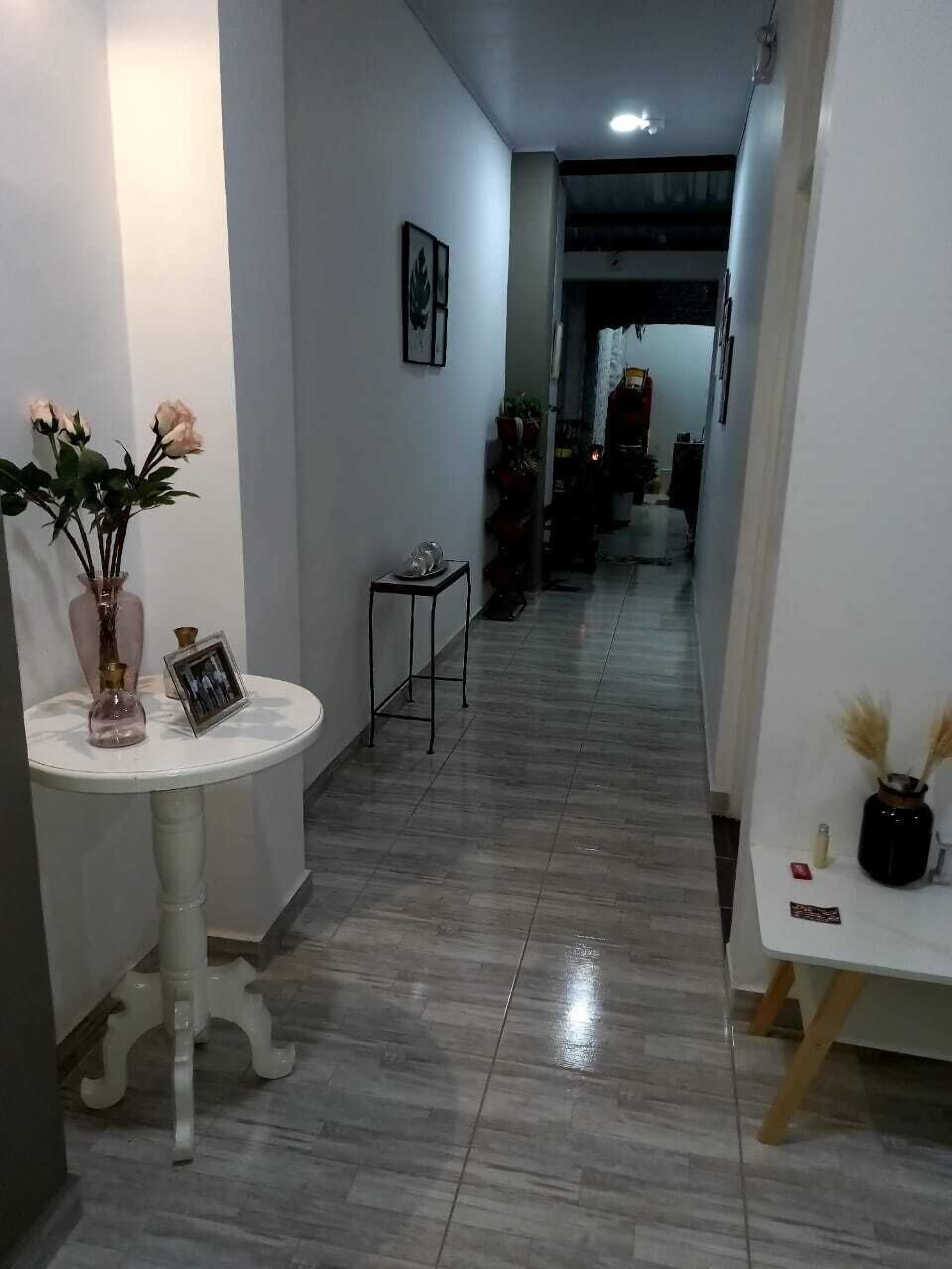 Um corredor com uma mesa redonda branca à esquerda, uma pequena mesa de apoio e um vaso com flores.