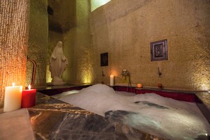Um quarto de spa com uma banheira de mármore cheia de bolhas, uma estátua e velas.