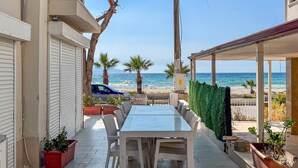 Um pátio com mesa e cadeiras, com vista para uma praia e o mar.