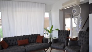 Sala de estar com um sofá cinza, duas poltronas, um sonho apanhado e um vaso de planta.