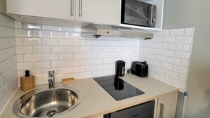 Uma cozinha compacta com armários brancos, uma pia de aço inoxidável, um preparador de café preto e um micro-ondas embutido.