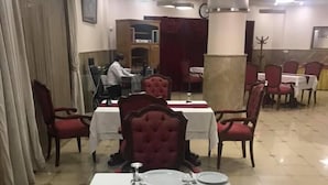 Uma sala de jantar com uma mesa comprida posta para quatro pessoas, cadeiras vermelhas estofadas e toalha de mesa branca.