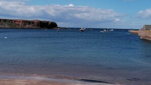 Cena costeira com barcos na água e um penhasco rochoso.