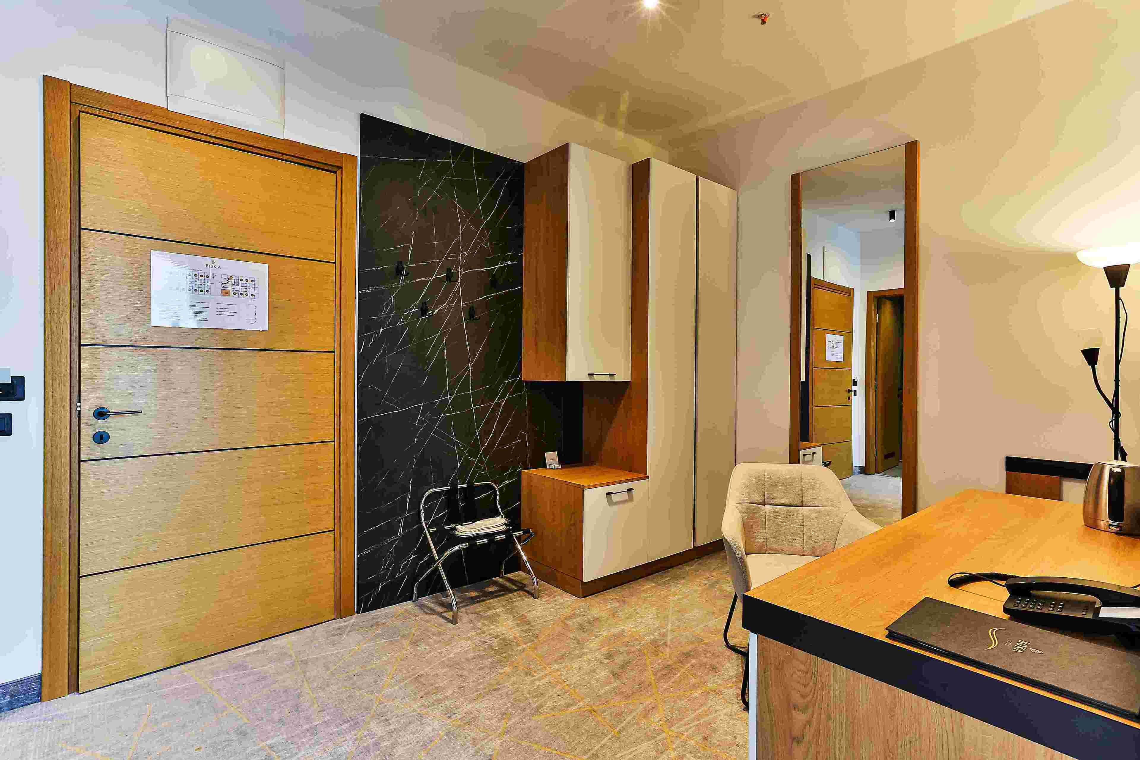 Quarto de hotel com guarda-roupa de madeira, parede de destaque em mármore preto, escrivaninha com telefone e uma cadeira.